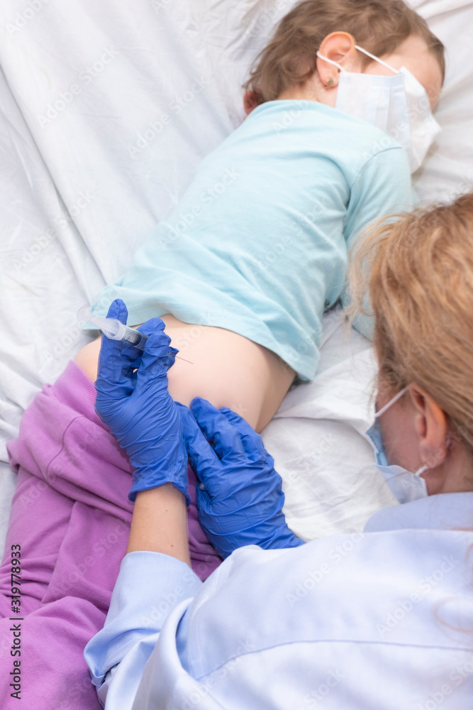 Pediatric nurse makes an injection in the baby’s bare buttock. Nurse's hands are holding a ...