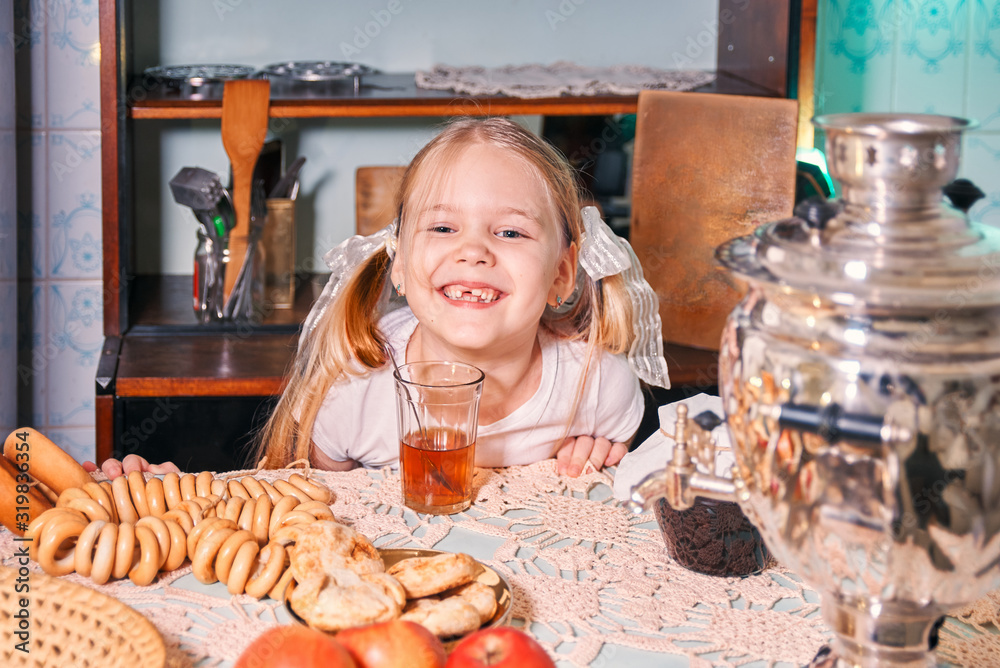 little girl drinks tea in the evening. on the table are buns, bagels ...