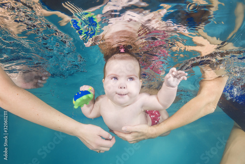 Cute chubby little girl plays with toy underwater in a swimming pool ...