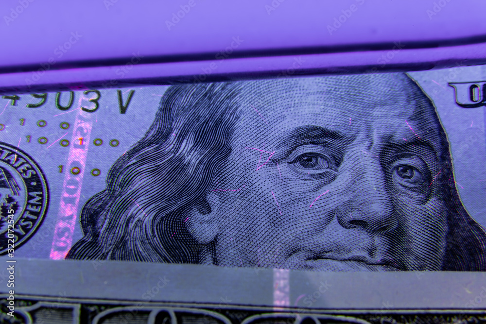 Extreme closeup on dollar banknote under ultraviolet light. Benjamin ...