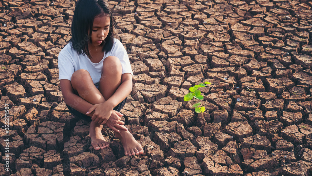 Fotografie Sad girl sitting on dry soil with small trees that grow ...