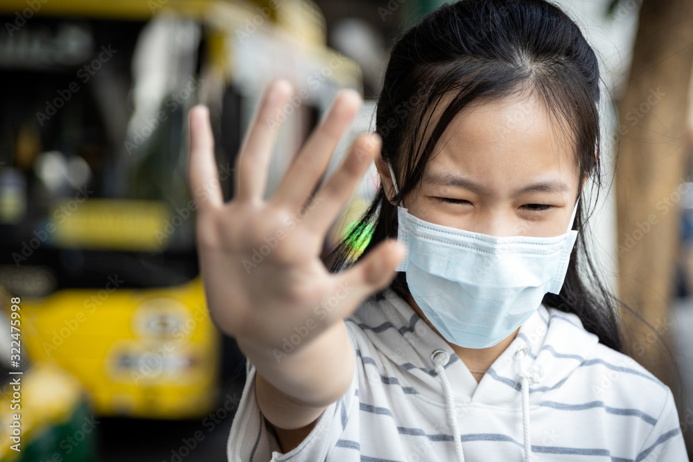 Asian child girl wearing protective mask at bus stop in the city,show stop gesture,hand"NO"sign ...