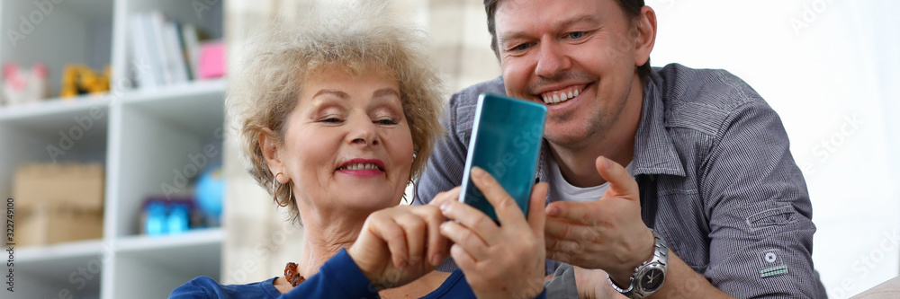 Millennial son helps an adult listen mother to master banking application in smartphone portrait ...