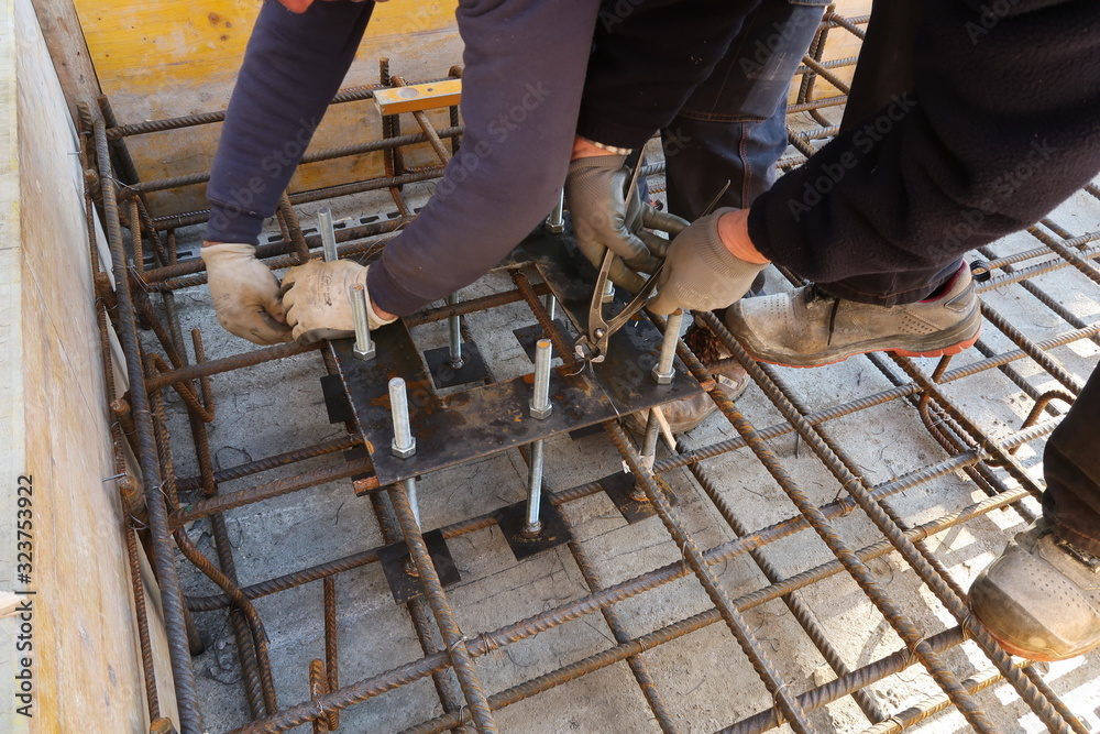 Workers mount steel plates with anchor bolts for columns on a ...