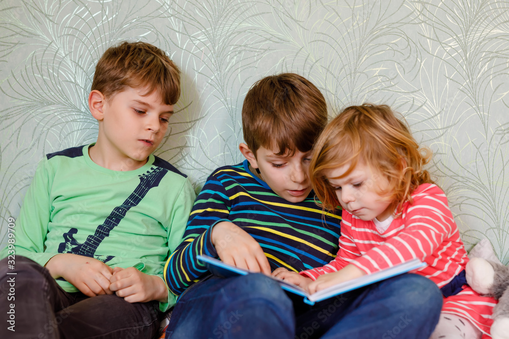 Two school kids boys and little toddler girl reading together book ...