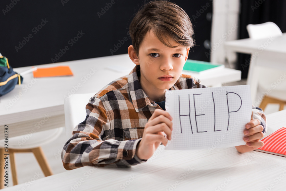 selective focus of upset schoolboy holding paper with help lettering ...