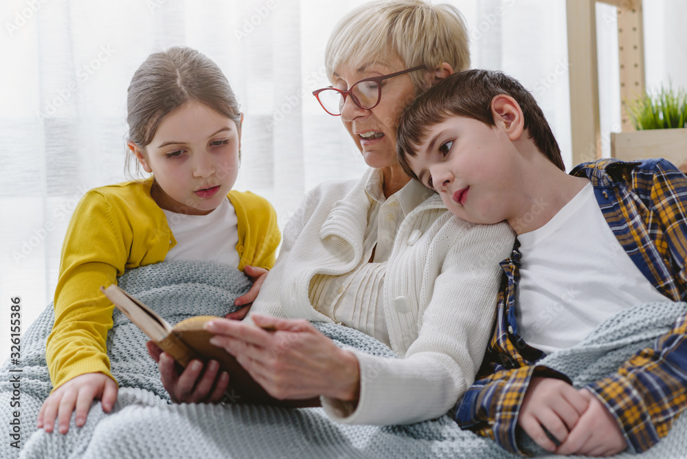 Grandmother reading a book to her grandchildren. Cute boy and girl ...