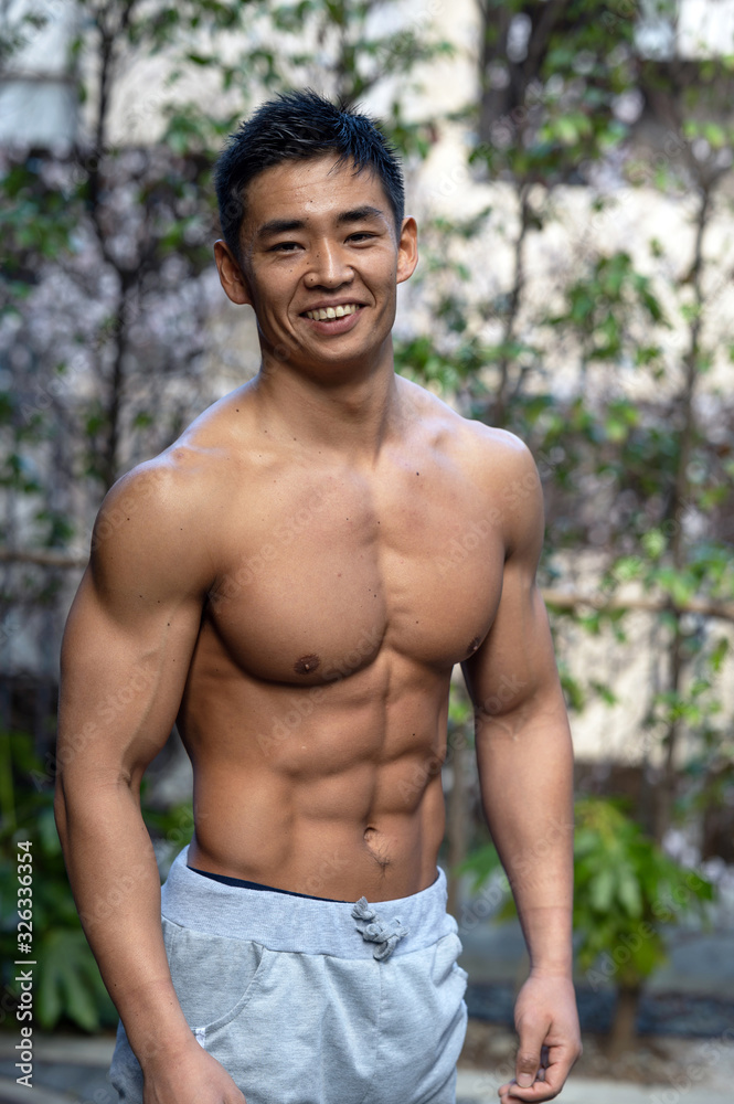 A young Asian amateur bodybuilder poses shirtless outdoors showing off ...