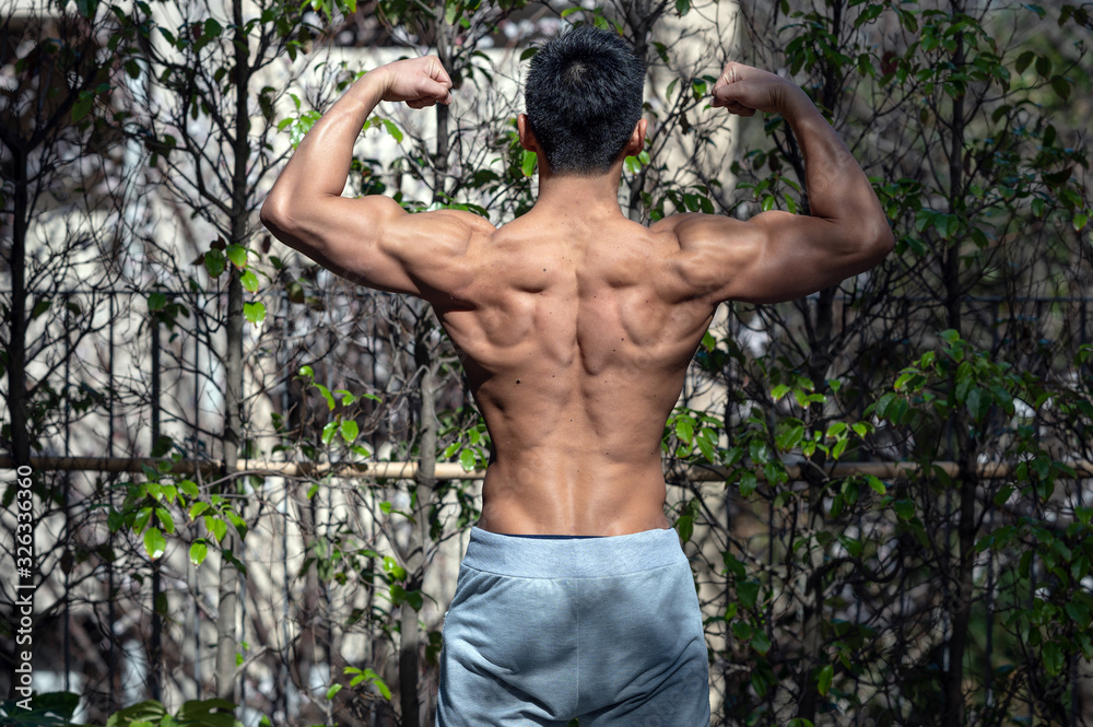 A young Asian amateur bodybuilder poses shirtless outdoors showing off ...