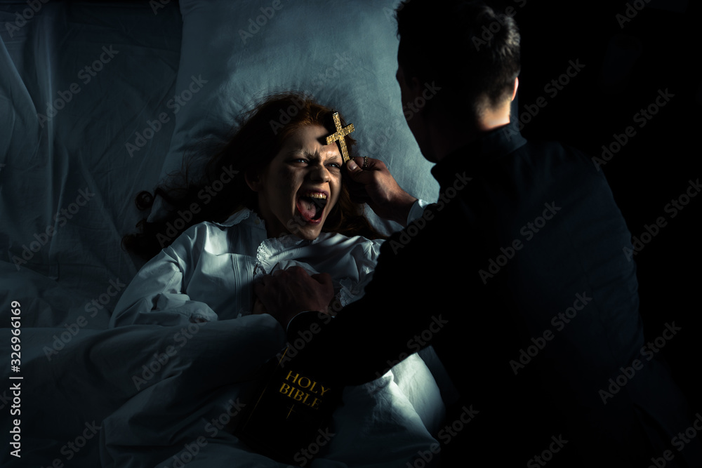 exorcist with bible and cross standing over demoniacal yelling girl in ...