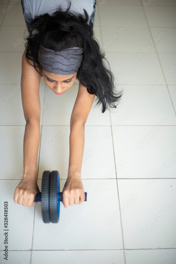 Indian brunette girl in sportswear performing exercise with ab roller ...