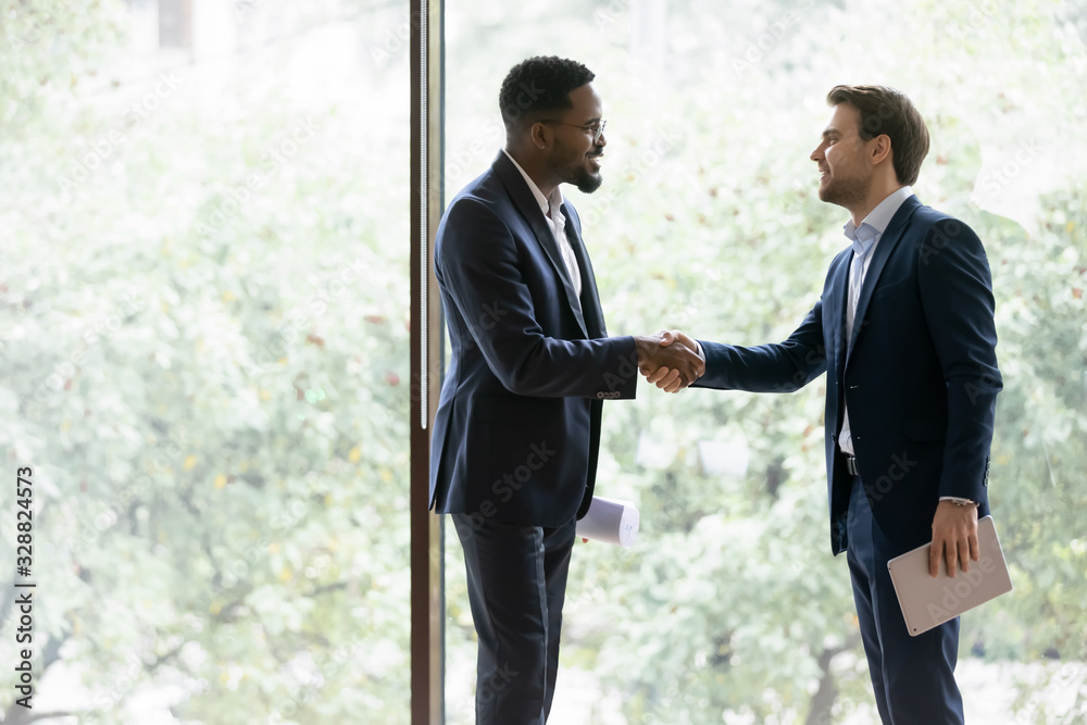 Happy multiracial male business partners shake hands get acquainted ...