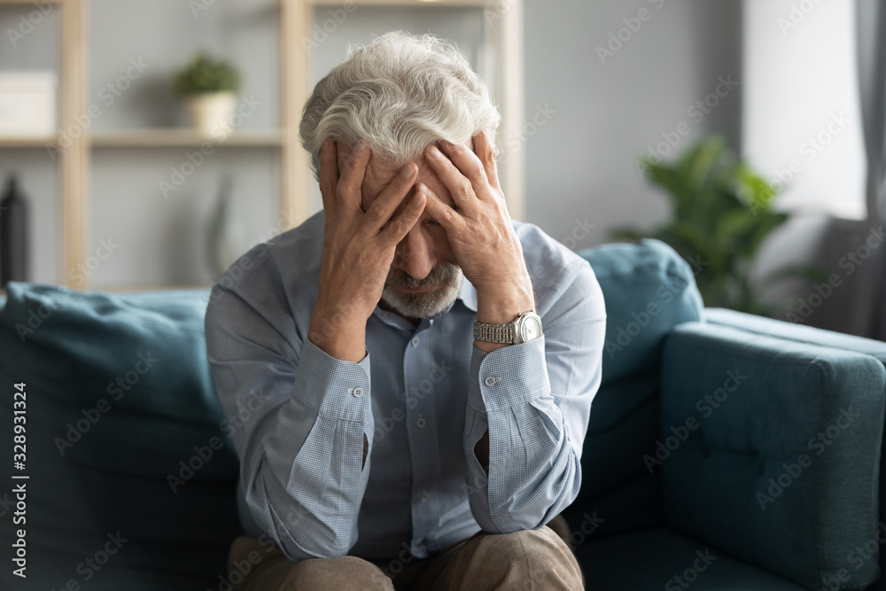 Depressed old 60s man sit on couch in living room feel lonely unhappy ...