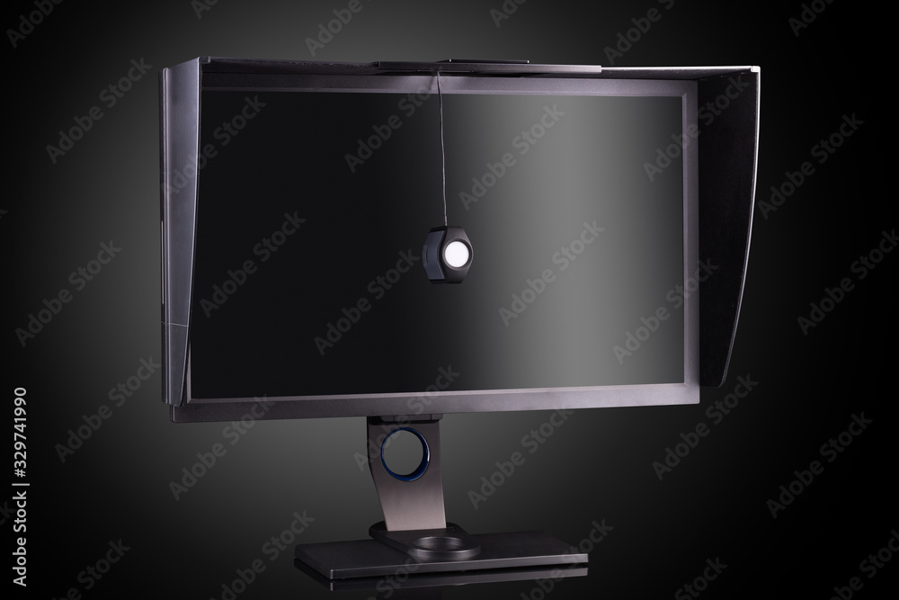 Professional monitor with shading hood and calibrator isolated on black ...