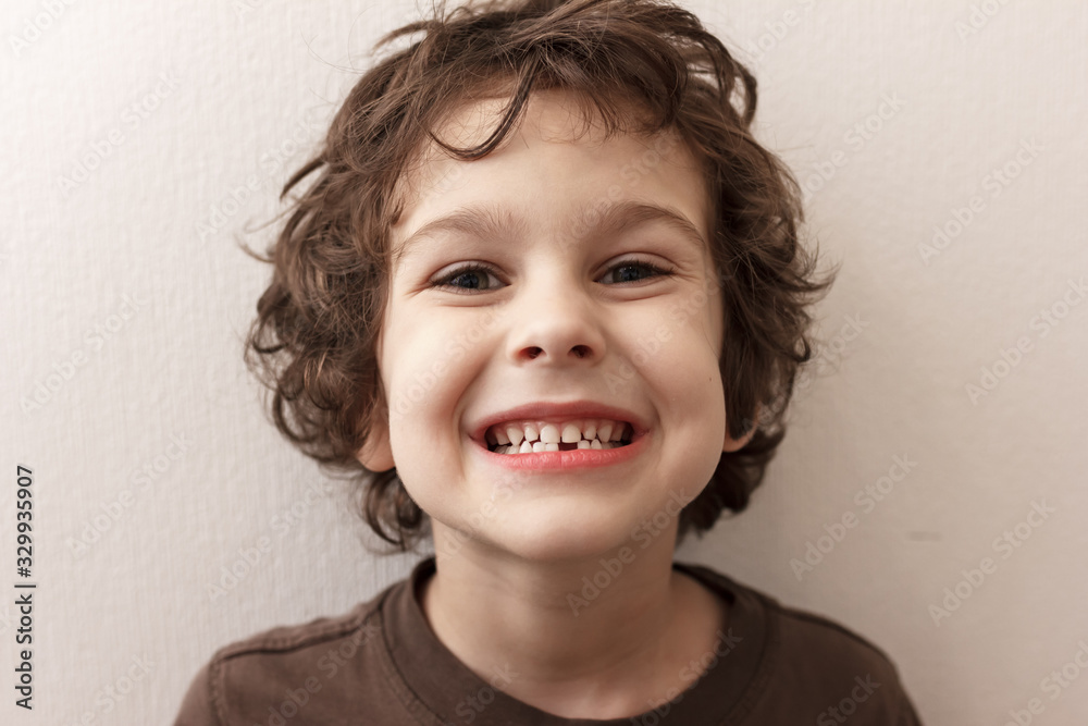Foto Charming curly boy smiles without tooth on white background. The ...