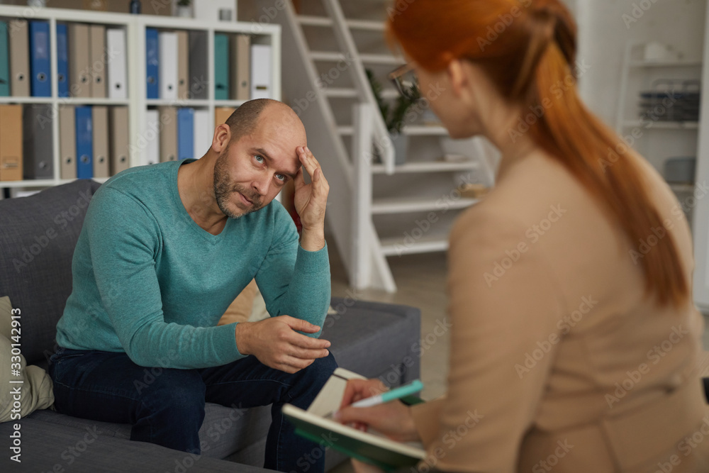 Mature man sitting on sofa and talking about his problems to ...