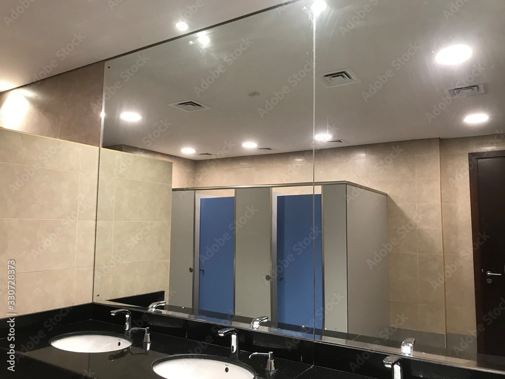 Big mirror image of toilet cubicles of an Men washroom and wash basin ...