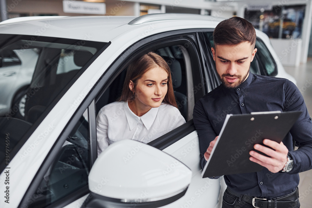 Woman testing car by help of male assistant that shows doments indoors ...