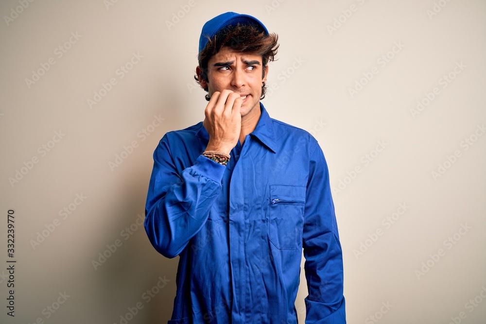 Young mechanic man wearing blue cap and uniform standing over isolated ...