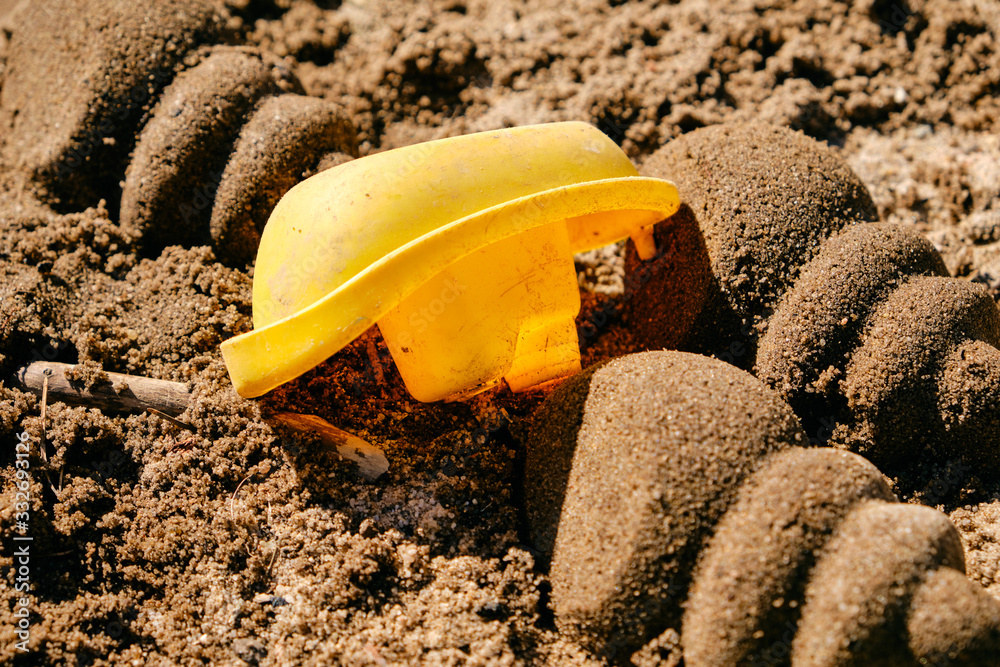 Used yellow toy boat lying upside down between sand shells on the sandy ...