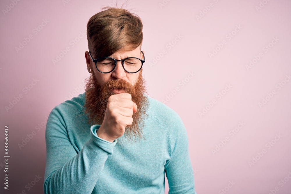 Handsome Irish redhead man with beard wearing glasses over pink ...