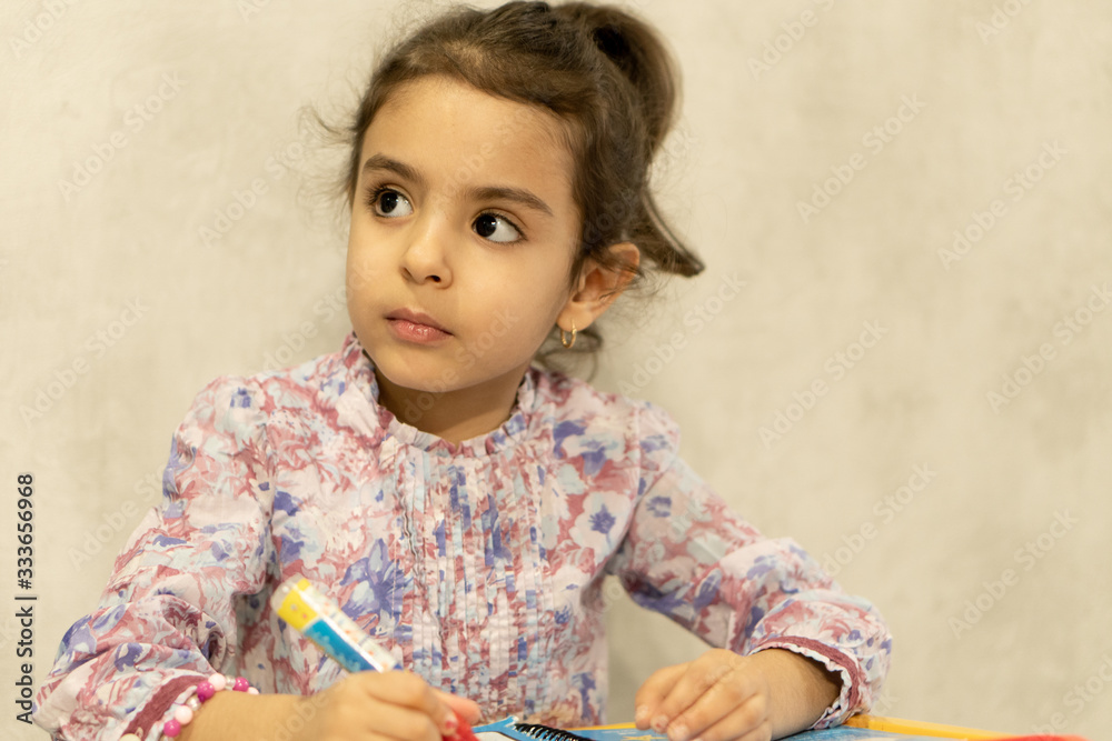 Little girl of Persian appearance draws sitting at desk. Beautiful girl ...