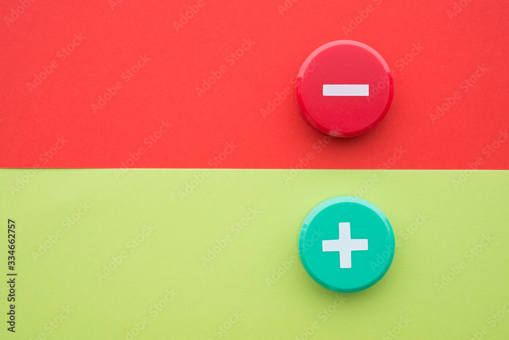 Flat lay of green plus and red minus symbol plastic botton on green and ...