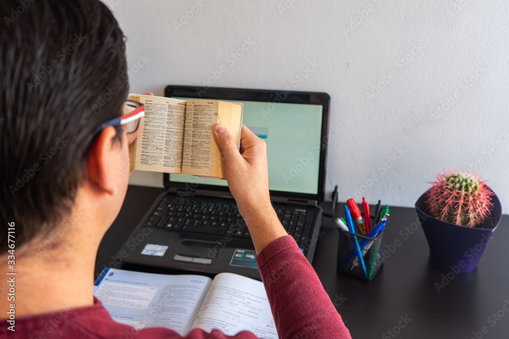 Man studying English. In his hands he has a dictionary. On the desk is ...