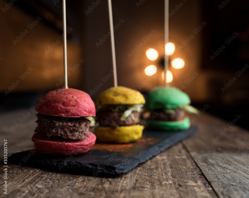 Mini hamburger colorati di manzo su piatto di ardesia, tavolo in legno ...