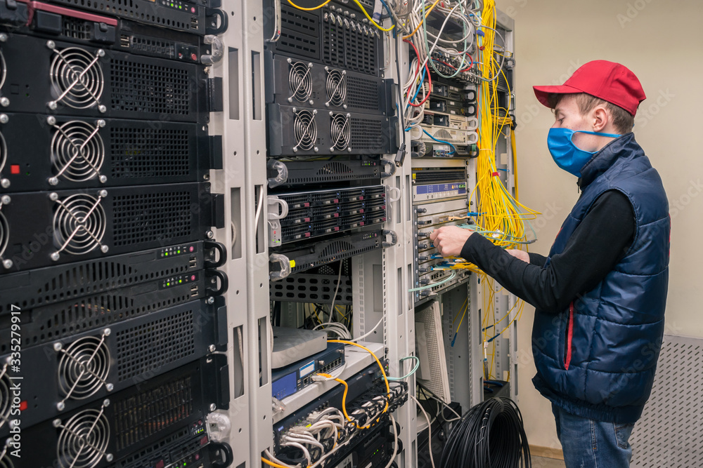 Young technician in medical mask switches fiber optic wires on the main ...