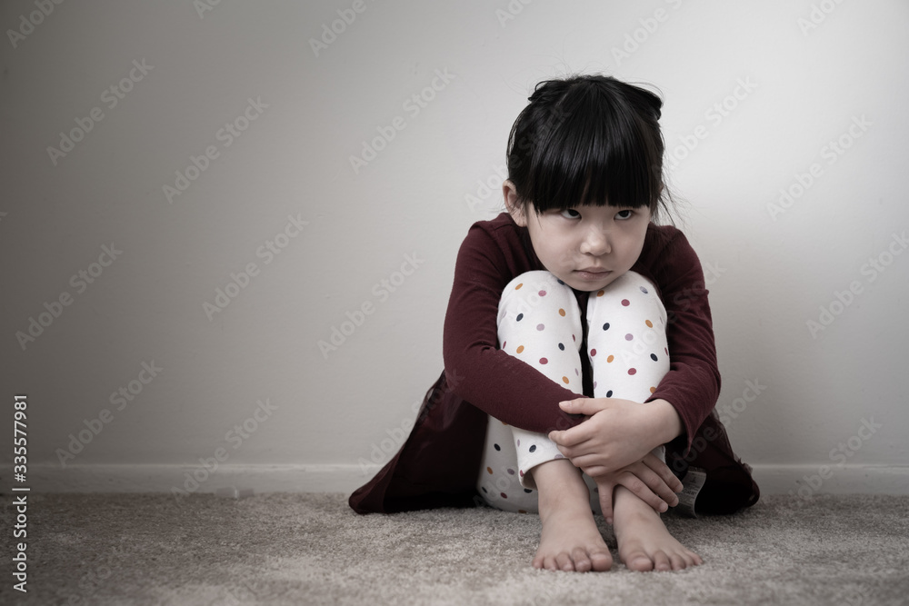 Lonely sad young girl is sitting in the corner wall and holding her ...