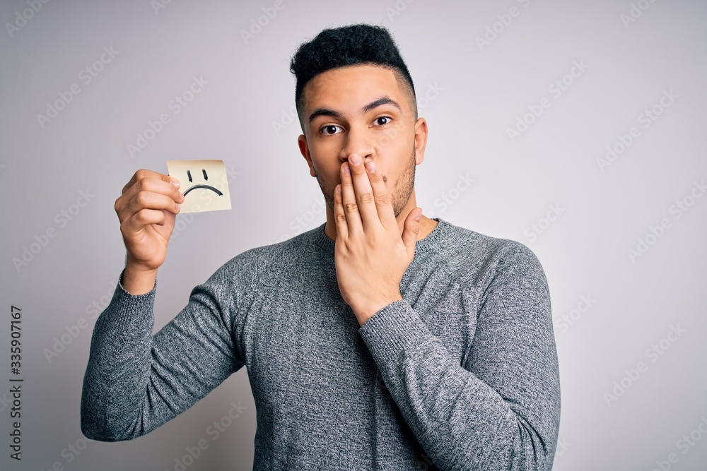 Handsome man holding reminder paper with sad emotion face emoji over ...
