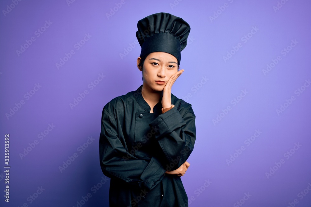 Young beautiful chinese chef woman wearing cooker uniform and hat over ...