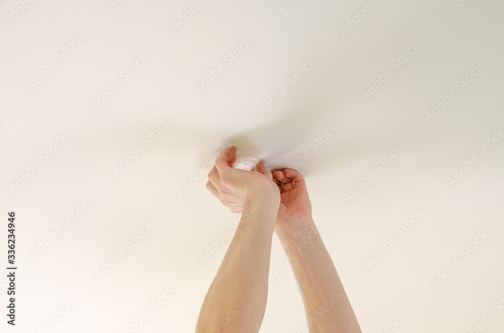 Men's hands cut a hole for a recessed spotlight in a suspended ceiling ...