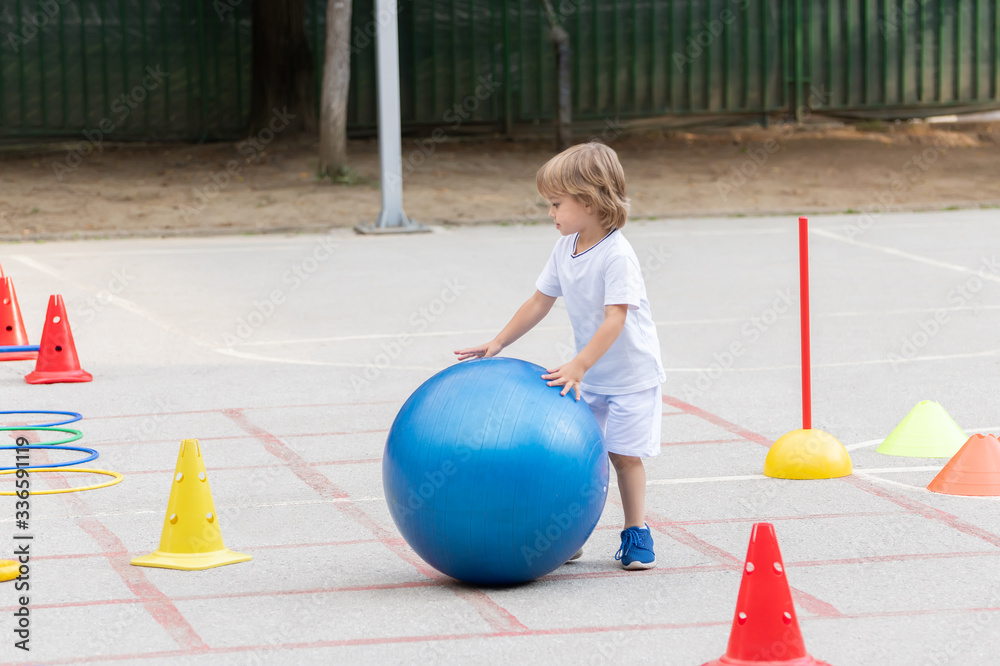 Beautiful little boy rolling the big blue ball on sports polygon Stock ...