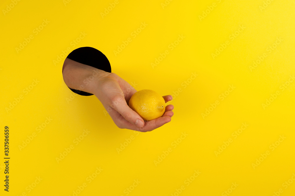 Hand in a hole on a yellow background and offers lemon as a source of ...