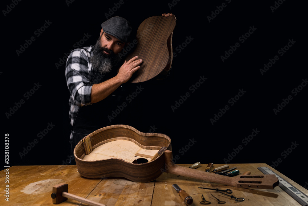 Luthier wearing cap, plaid shirt and apron. Hearing the resonance of ...