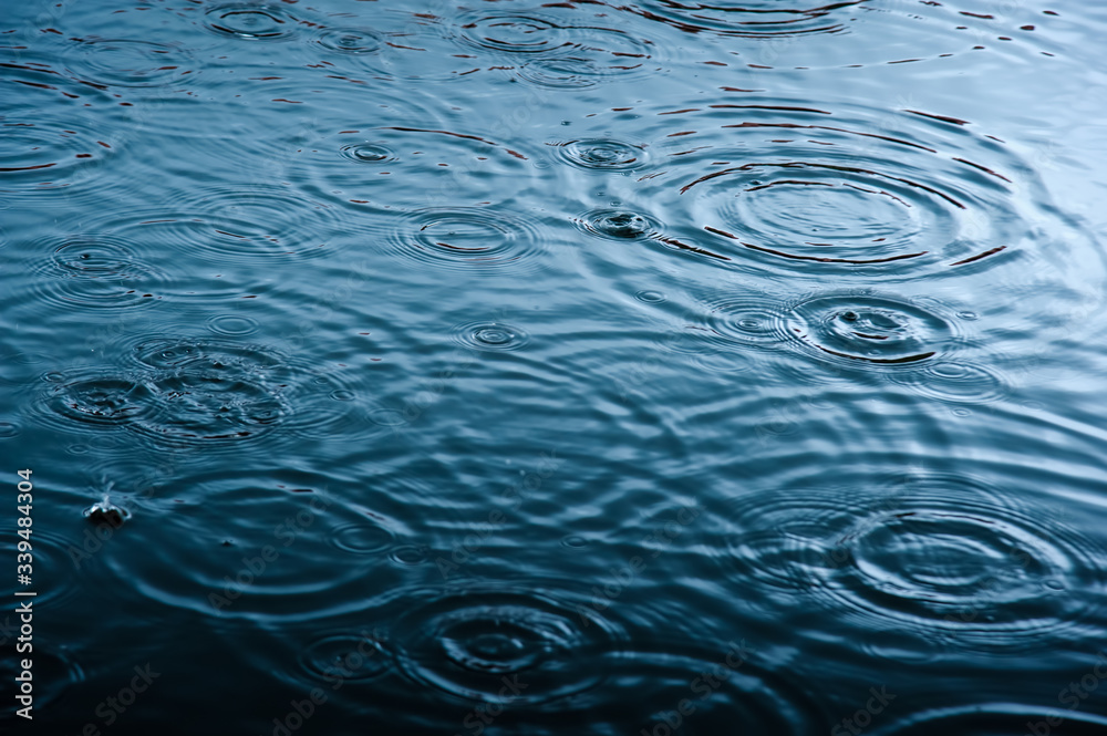 rain drops on the surface of water in a puddle with graduated shade of ...