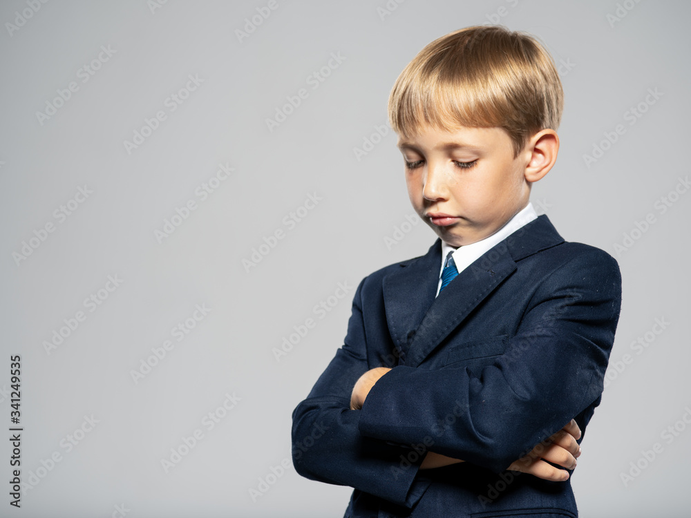 Sad blond boy dressed in a formal suit with blue tie looking down ...