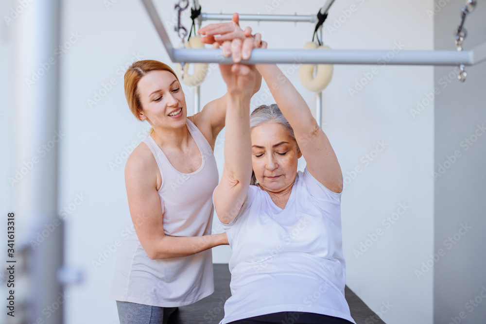 Older woman doing exercise on pilates chair equipment. Young female ...