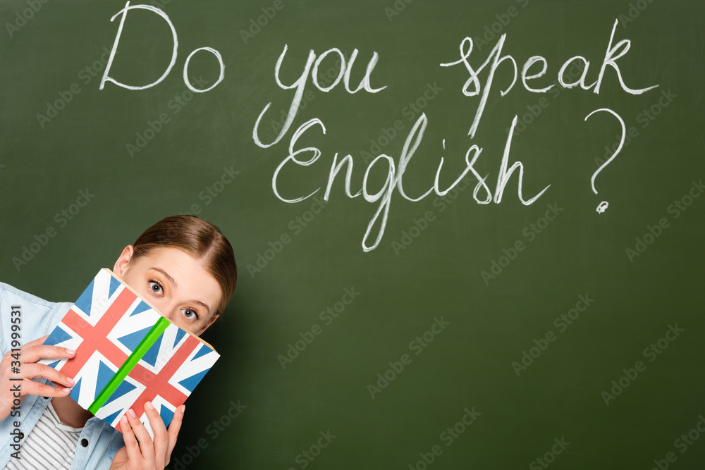pretty girl with obscure face holding book with uk flag near chalkboard ...