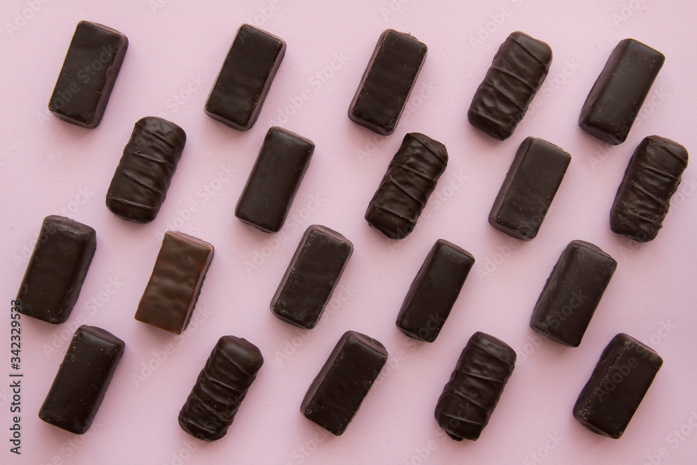 Chocolate candies lie in a row without candy wrappers on a pink ...
