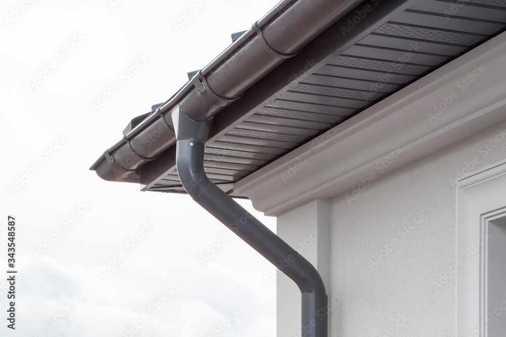 Corner of the house with new gray metal tile roof and rain gutter ...