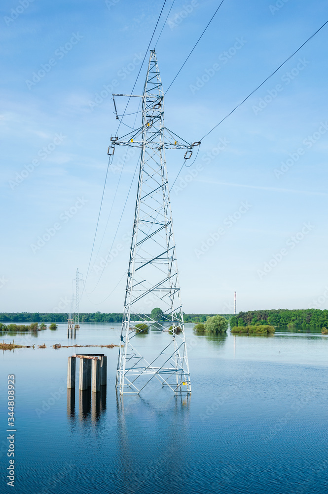 The high voltage power lines on water. Blue sky and green trees during ...