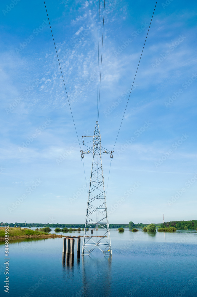 The high voltage power lines on water. Blue sky and green trees during ...