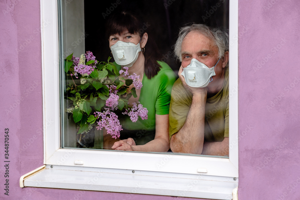 The older couple hug. loving woman and man look out window in masks ...