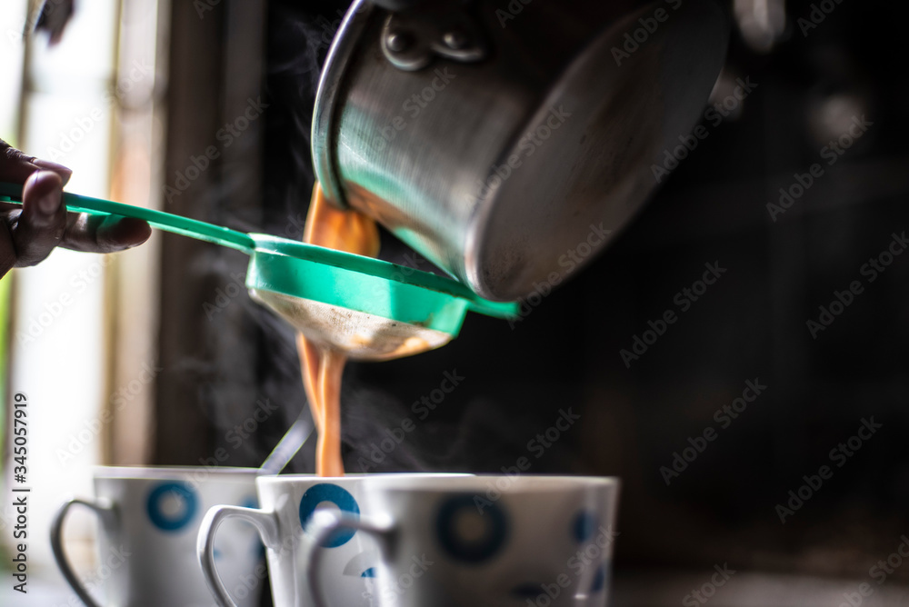 Tea being strained and poured into the cups from an aluminium tea pot ...