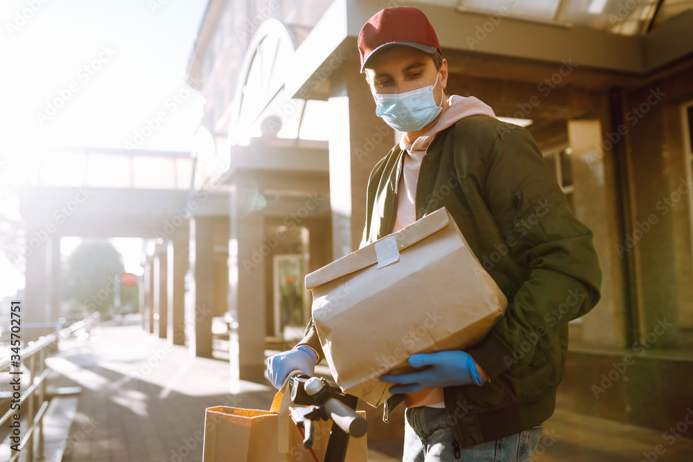 Courier in protective mask and medical gloves on a scooter delivers ...