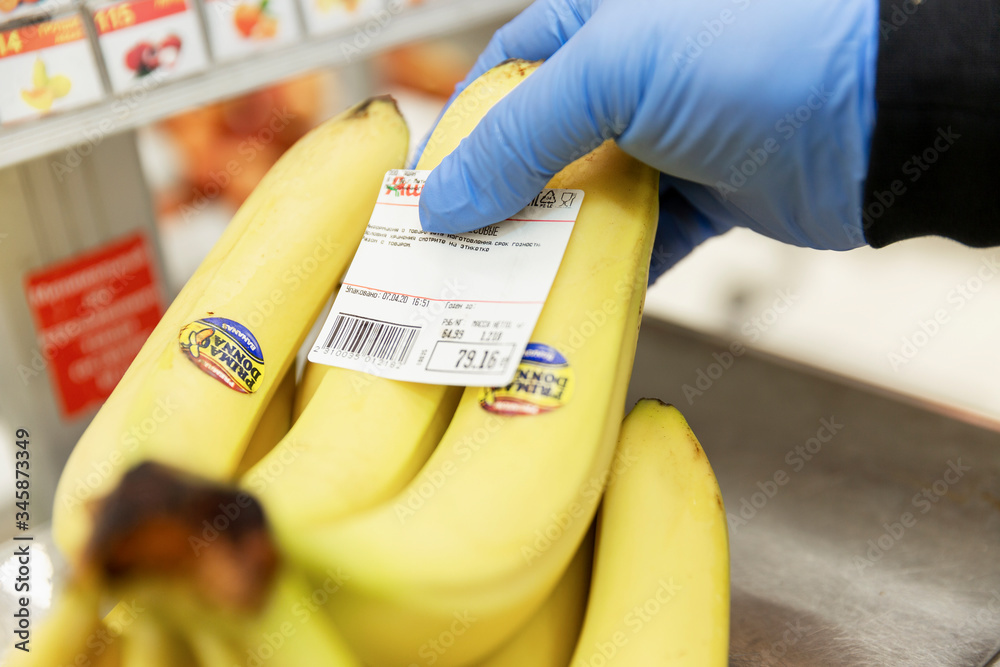 Hand in a glove placing a price tag on bananas at a supermarket. Close ...