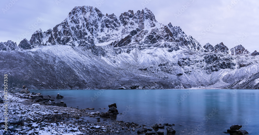 Rocky shoreline of high-altitude Gokyo Lake with snow-capped mountains ...